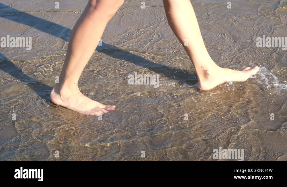 Woman or girls legs walking barefoot on beach coastline in shallow ...