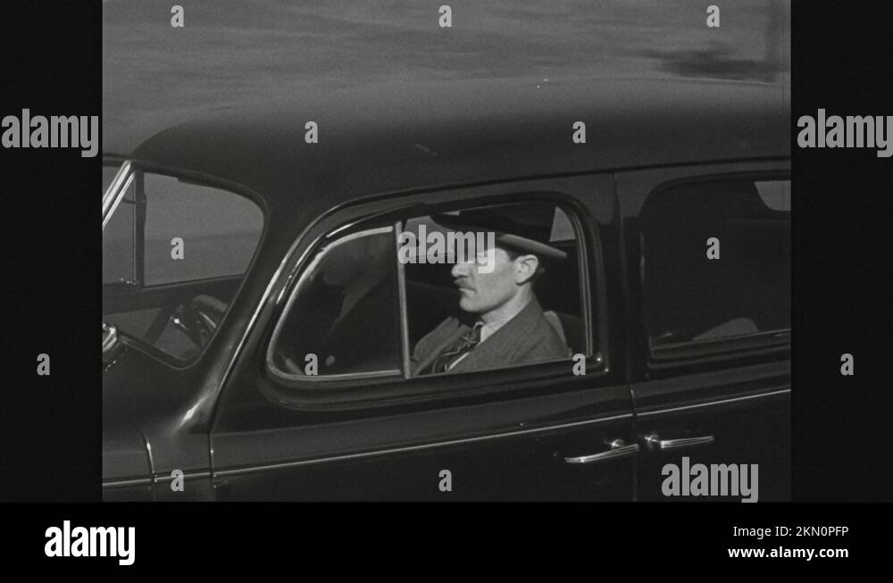 1940s: Man through car window driving next to ocean lined with large ...