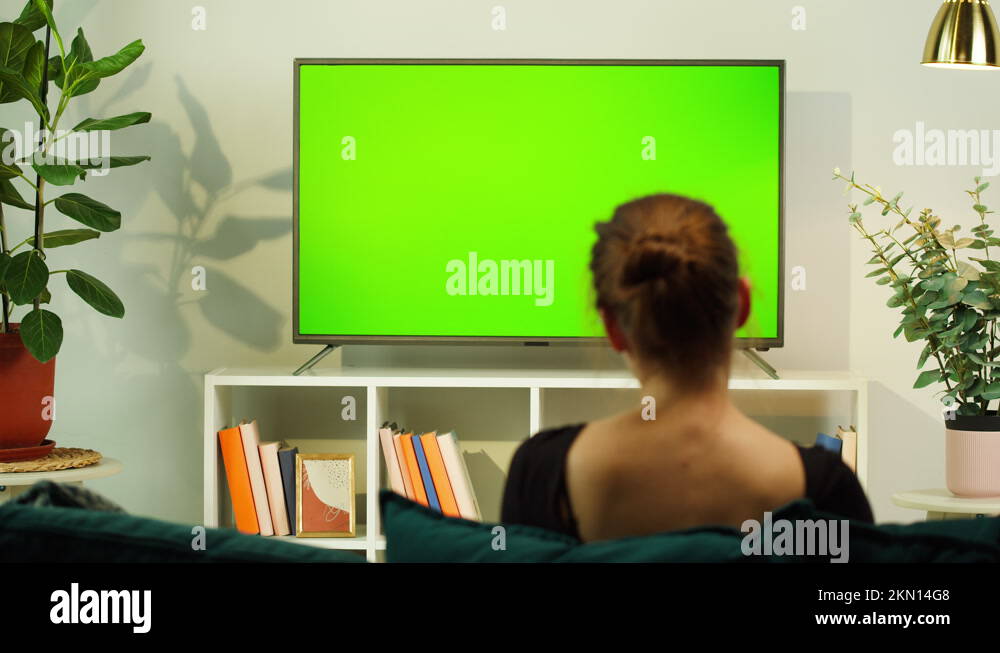 Woman watching TV with green screen in living room back view. Female ...