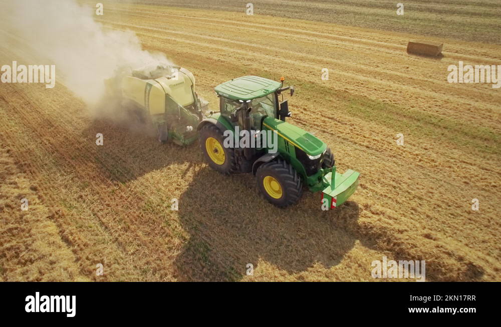Tractor towing straw baler working on field, compressing straw to large ...
