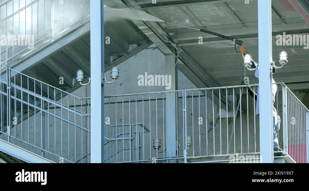 Maintenance worker cleaning metal stairs using water pressure washer ...
