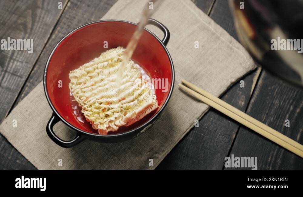 Boiling water pouring into red bowl with instant noodles with spices ...