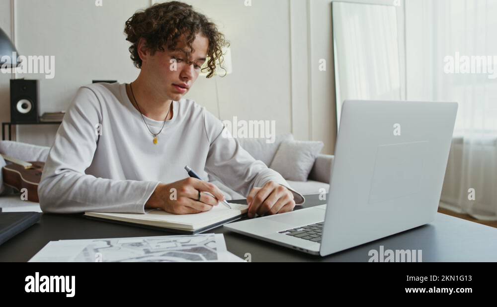 Handsome man makes notes in a notebook while sitting in front of open ...