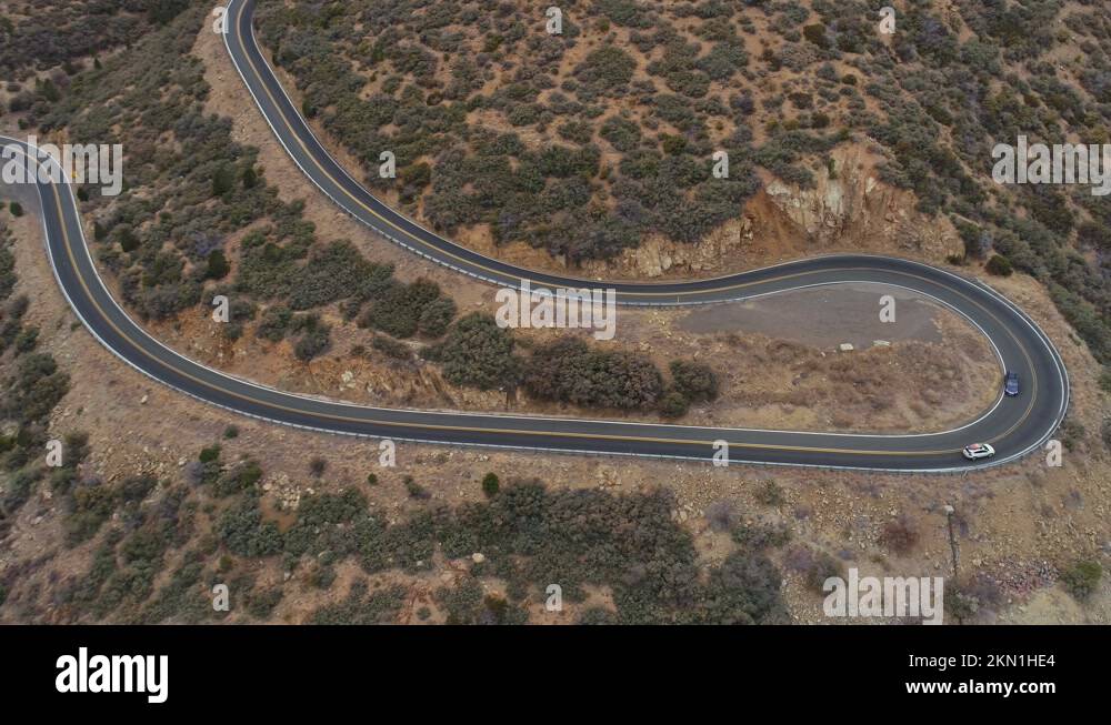 Orbiting aerial as cars take sharp switchback turn on mountain highway ...