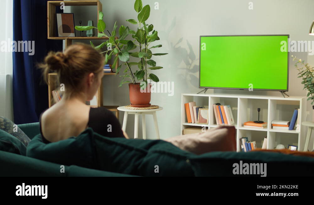 Woman watching TV with green screen in living room back view. Female ...