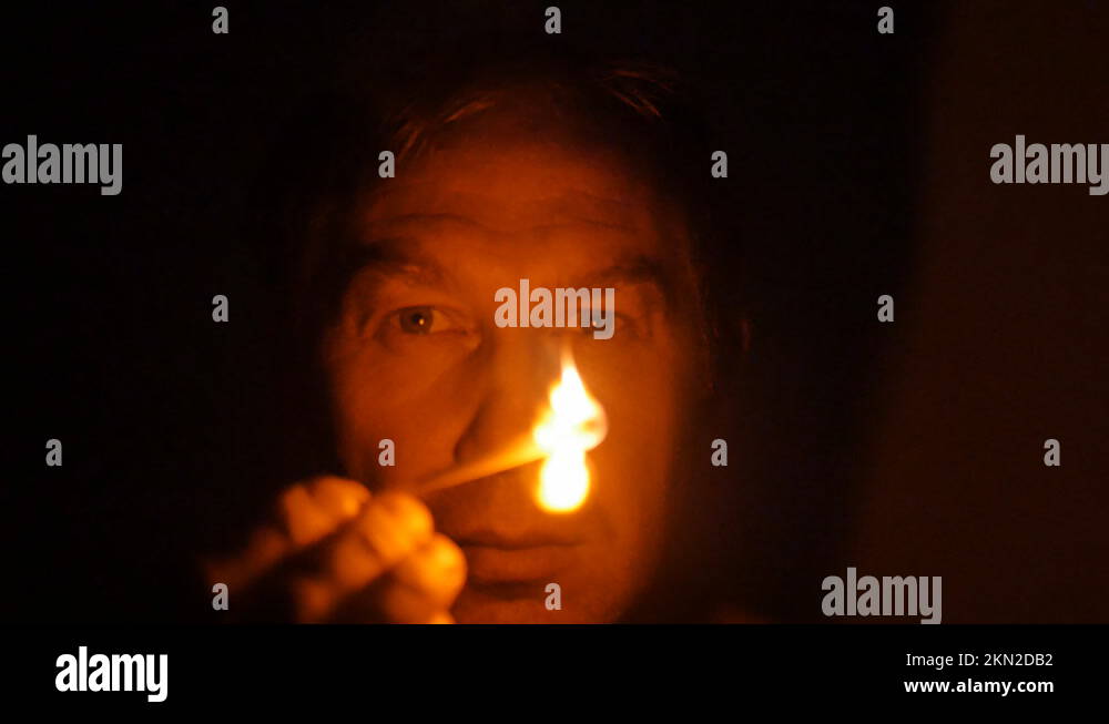 The man lit a match in the dark. The person's face is lit by fire from ...