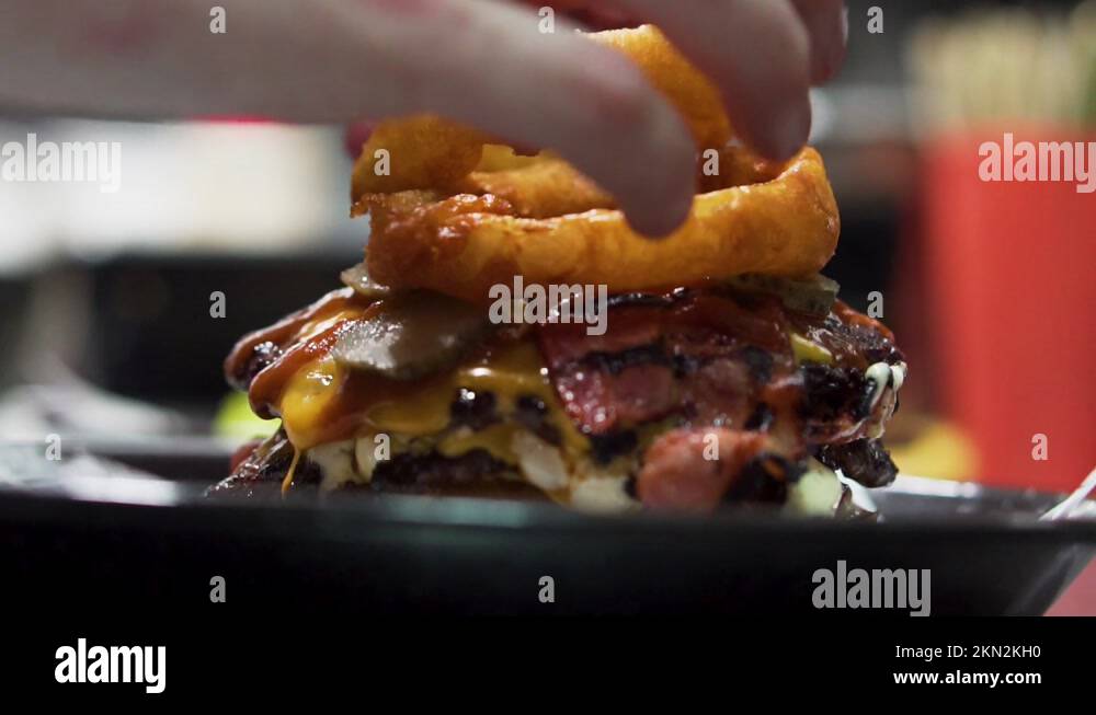 Chef assembling a big luxury burger filled with bacon and onion rings ...