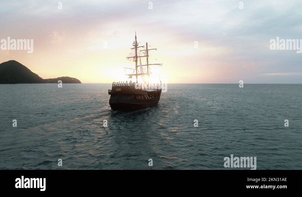 Cinematic back view of historic ship sailing toward scenic pink golden ...