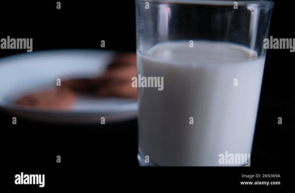Blurry plate of cookies behind glass of milk with black background ...