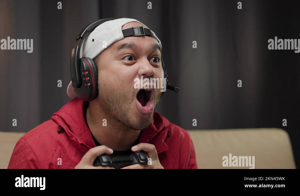 Excited and shocked face of Asian gamer with headphone holding joystick ...