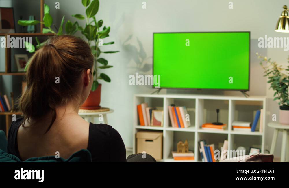 Woman watching TV with green screen in living room back view. Female ...