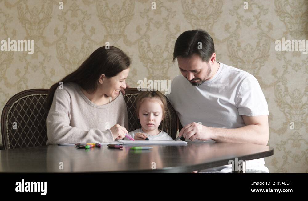 Family education. A little girl, with her parents, draws with colored ...