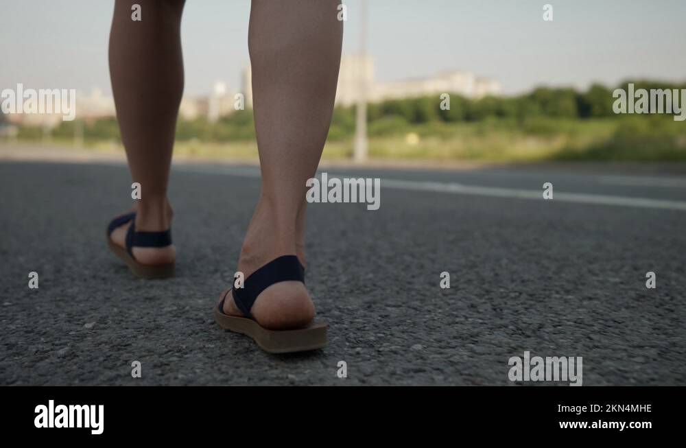 female feet in black sandals are walking on an asphalt path. close-up ...