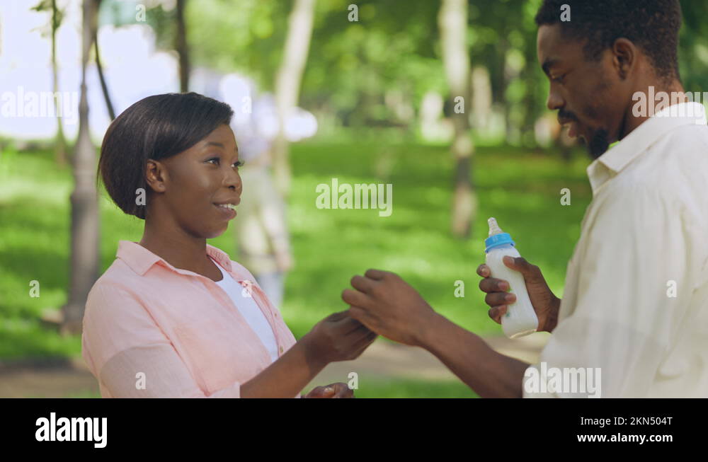 Woman giving rattle and milk bottle to young father, first time alone ...