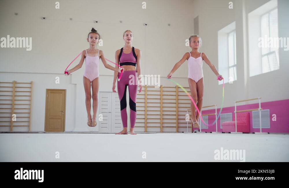 Gymnastic training - two little acrobatic girls jumping over the rope ...