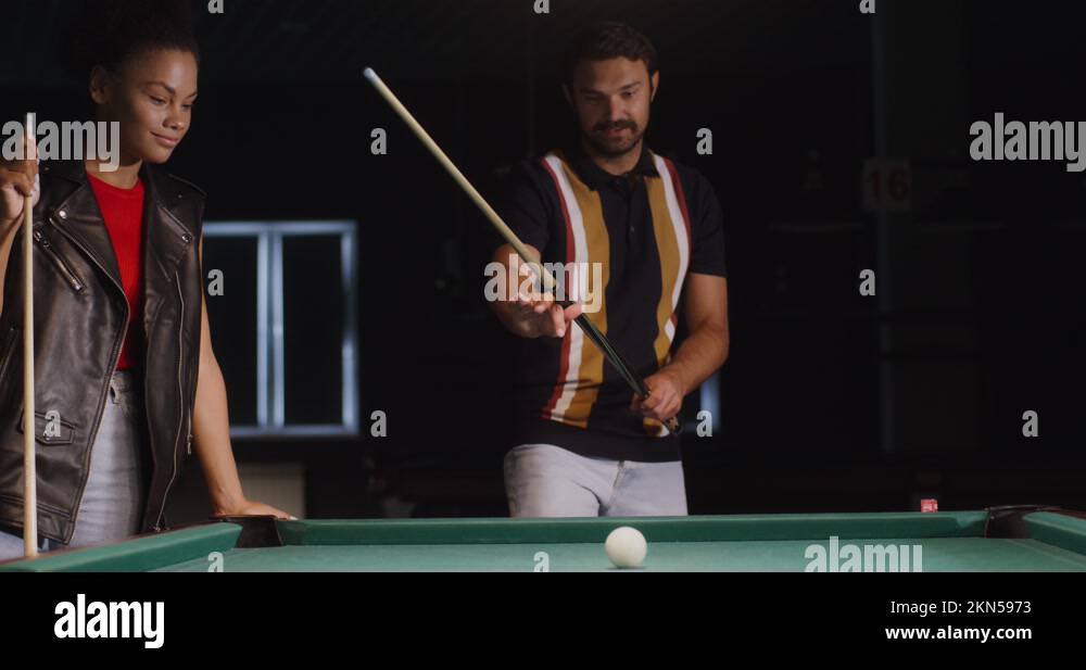 A man shows woman how to hold a cue and break a triangle in billiards ...