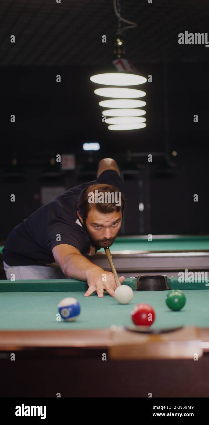 A man intently aims and hits billiard ball with a cue, driving it into ...