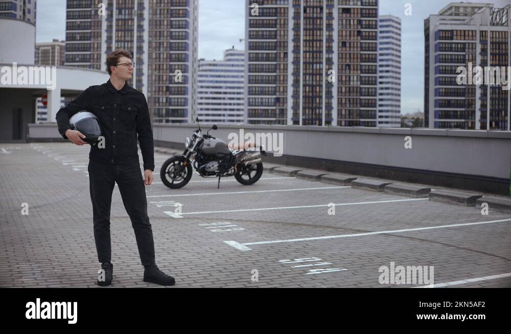 Smart guy stands in front of motorbike with helmet at top of multi ...