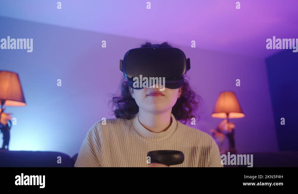 Pretty young gamer girl with curly hair sitting on couch and wearing ...