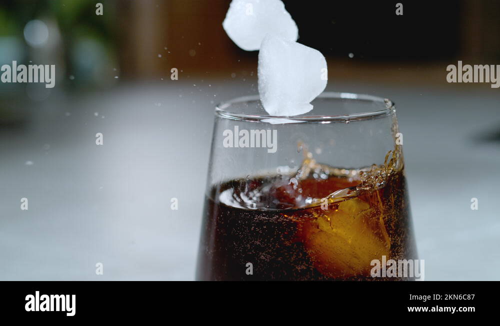 CLOSE UP: Odd shaped ice cubes fall into a vintage glass full of fizzy ...