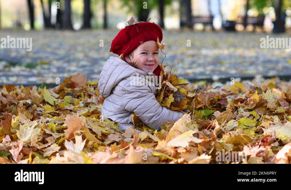 little girl walking in the park in the city throws yellow maple leaves ...