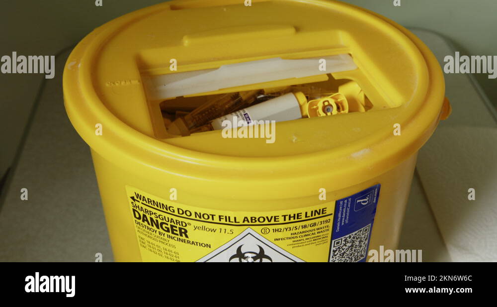 A hand disposing off a big syringe into a yellow medical waste ...