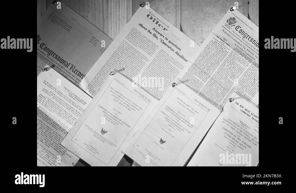 1960s: Newspaper clippings pinned to board. Men talking at a desk. Man ...
