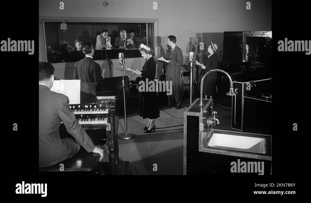 1940s: Radio station studio. Man in booth talks to actor and actress ...