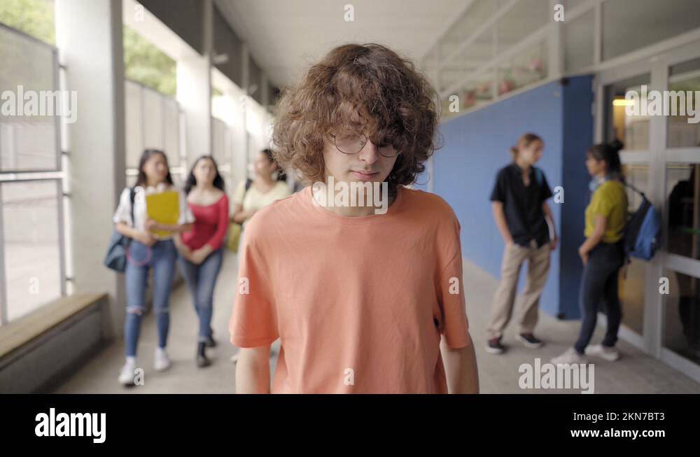 A teenage boy is standing in the high school hallways and some bullies ...