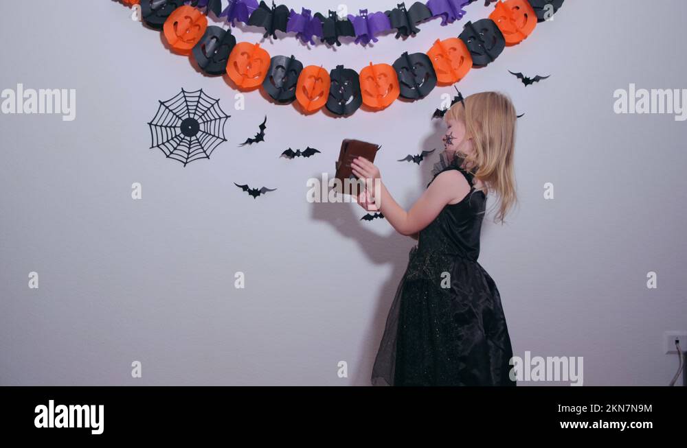 Little Girl in witch costume uses mobile phone to make video calls and ...