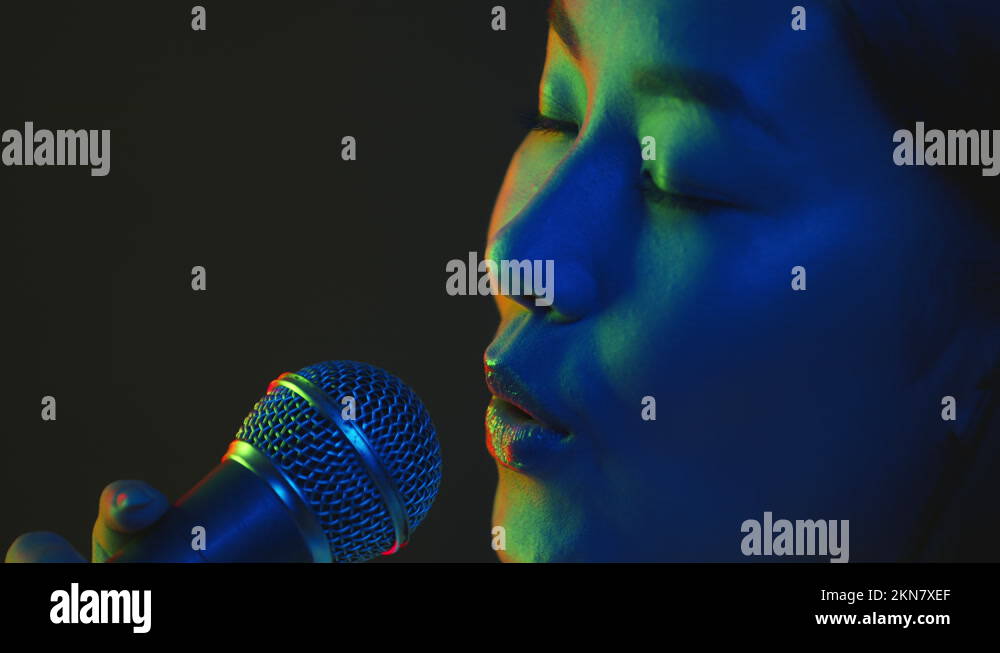 Young happy asian woman singer singing into mic in bright neon lights ...