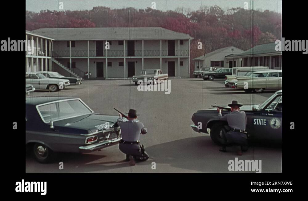 1960s: Police officers crouch behind police cars. Sedan stops in ...