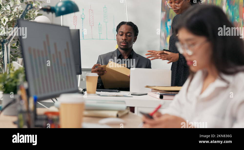 A busy dark-skinned boss in suit sits behind desk at a computer, an ...