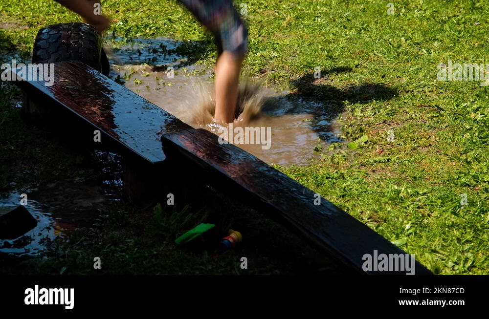 Twins having fun by jumping into muddy puddle, big splash, static shot ...