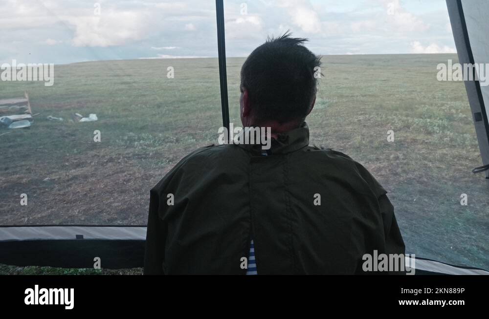 Back view of mature man sitting inside camp tent and watching nature of ...