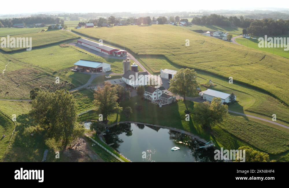 Cinematic aerial of family farm. Rural farmland. Pond, farmhouse, barn ...