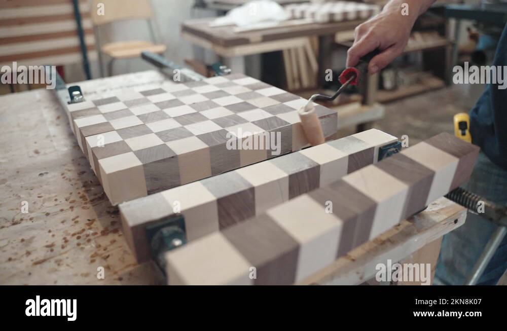 Craftsman using small platen for applying glue on sides of wooden bars ...