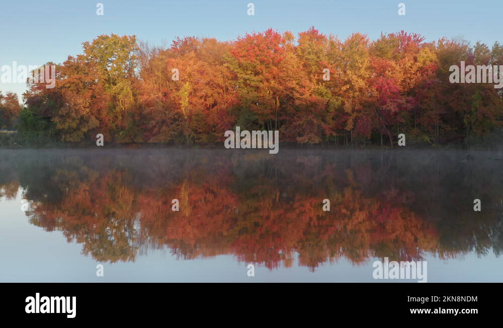 Cinematic fall foliage forest reflecting in the still surface of lake ...