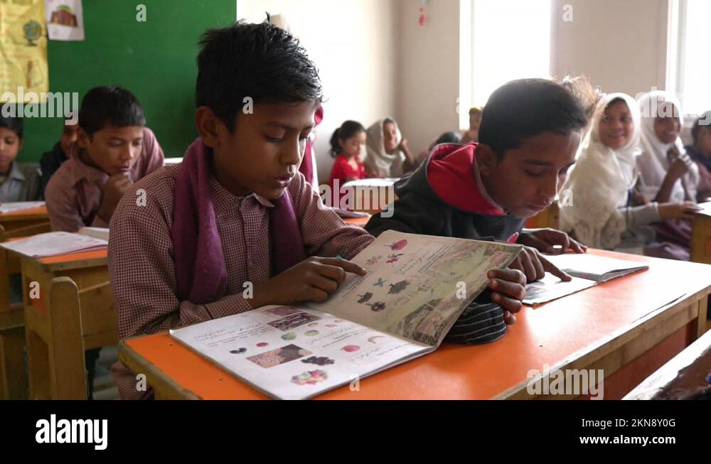 Two Young Muslim School Boys Reading Book At Desk In Classroom In ...