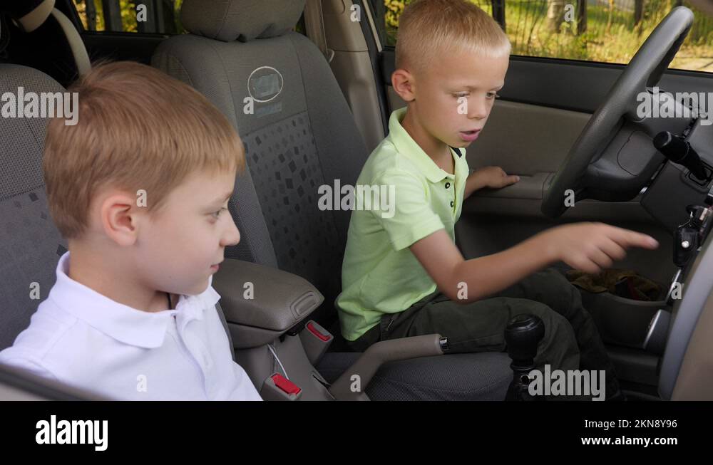 Curious kids are sitting behind the wheel in Dad's car and pushing ...