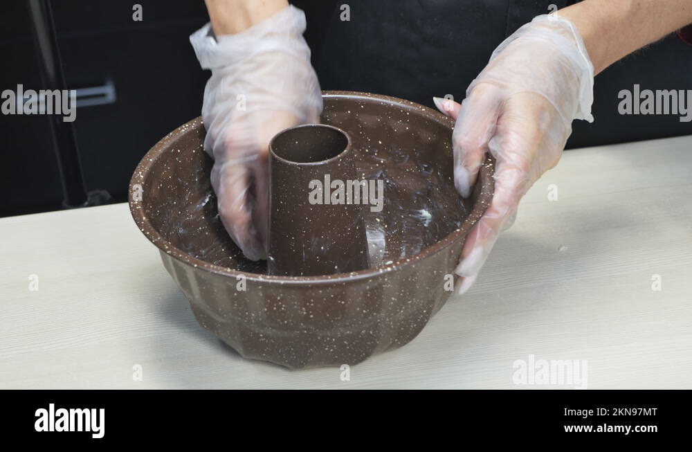 Gloved hands of a pastry chef butter the surface of a donut-shaped cake ...