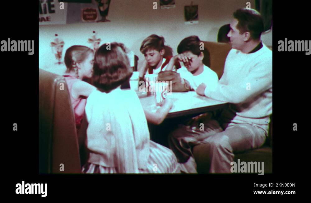 1950s: Malt shop. Man joins children in booth. Man puts his arm around ...