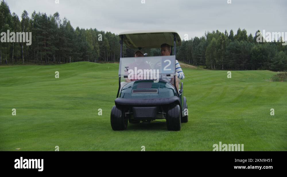 Two men drive electric car across a golf course, chatting with each ...