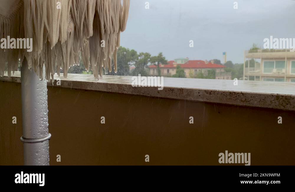 Raindrops fall on the parapet and folded parasol on the balcony. Slow ...