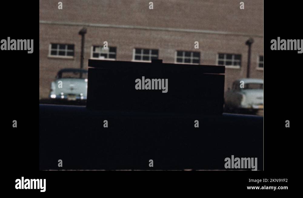1950s: Rear window view of car pulling away from brick building. Car ...