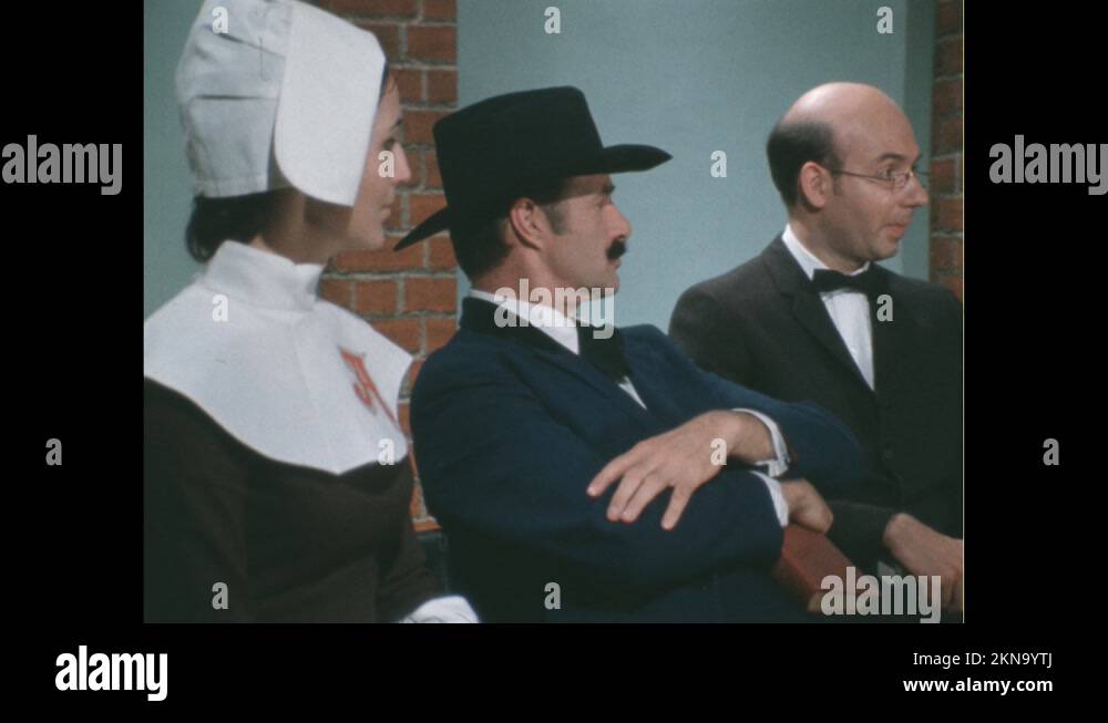 1970s: Three actors in costume sit on stage holding books. Film slate ...