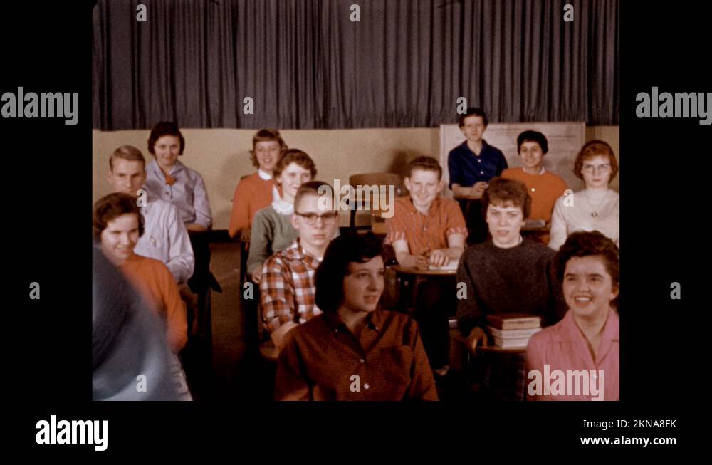 1950s: Slate. Classroom full of students listen. Teacher hands out ...