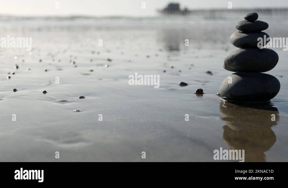Rock balancing on ocean beach, stones stacking by sea water waves ...