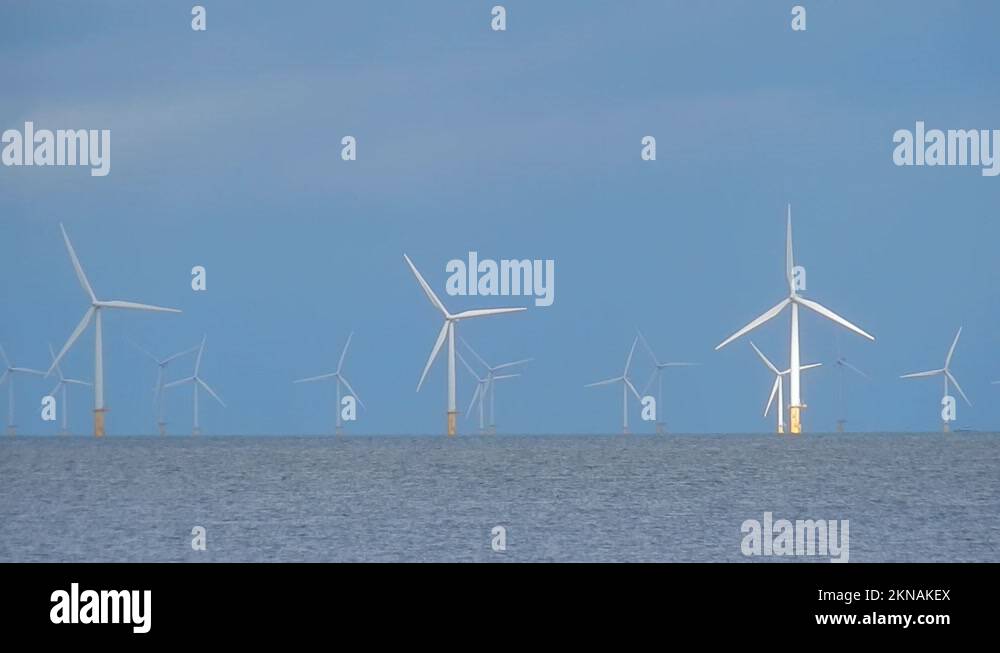 Row of offshore wind turbines with rotating blades along ocean horizon ...