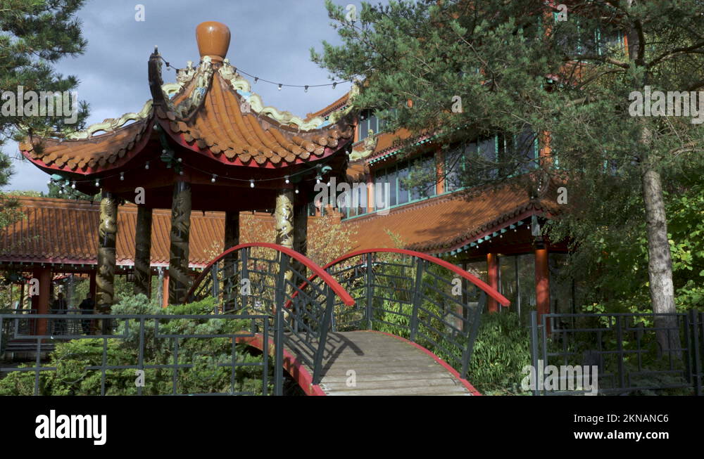 An arched bridge which crosses over a pond to join an Asian style ...